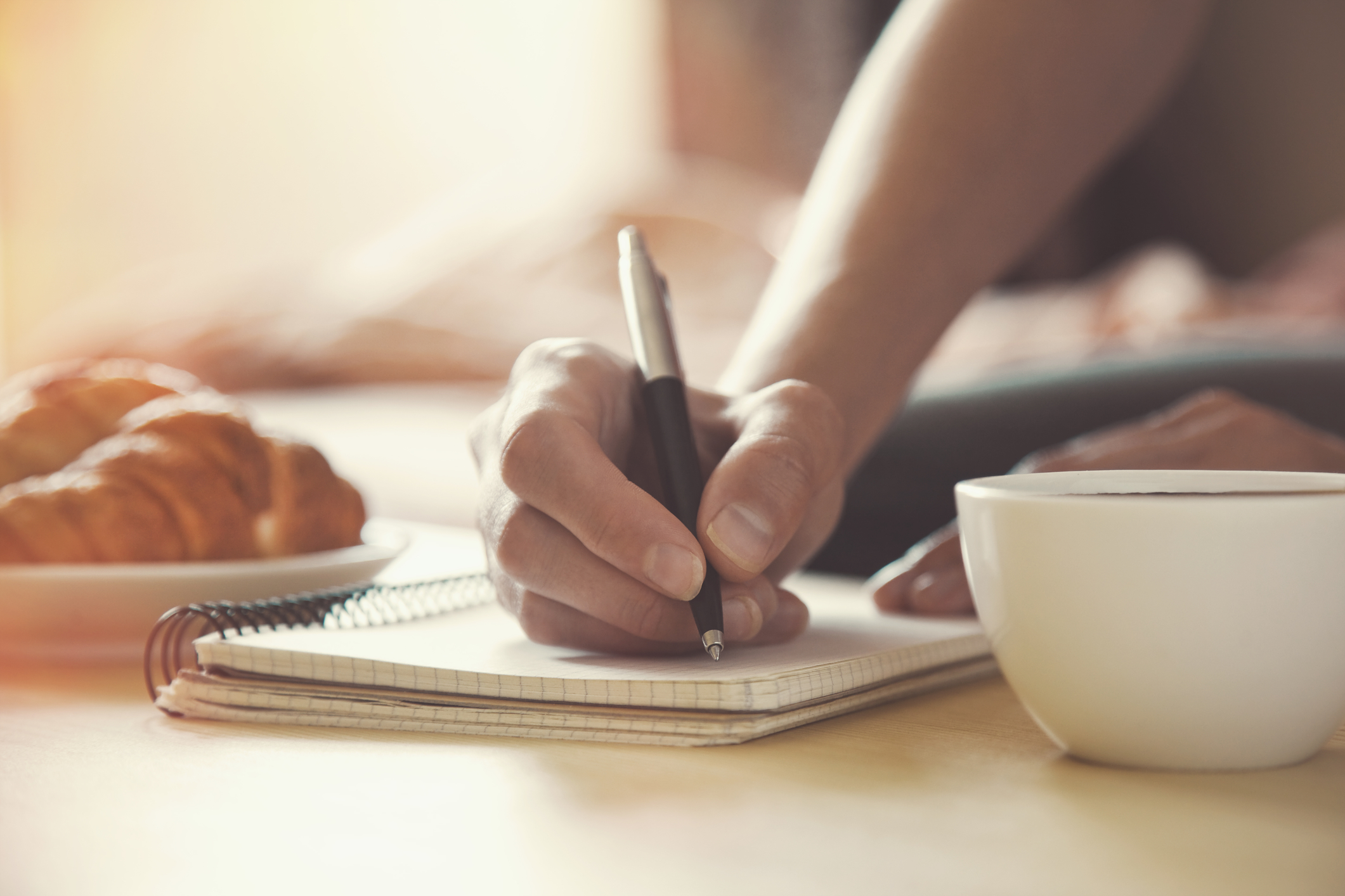 female hands with pen writing on notebook with morning coffee and ...
